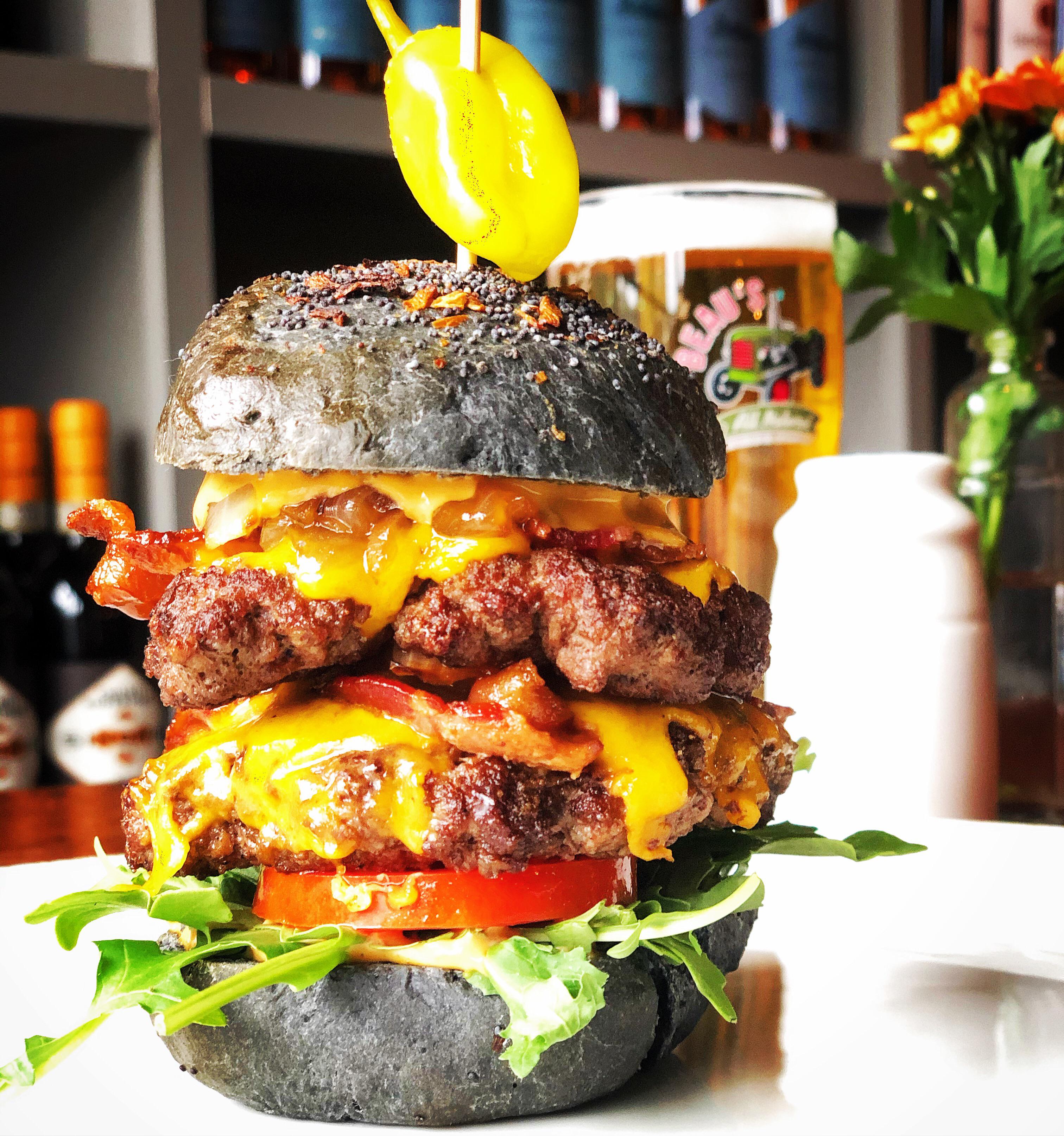 Double stack burger on charcoal bun with bacon, cheddar & caramelized ...